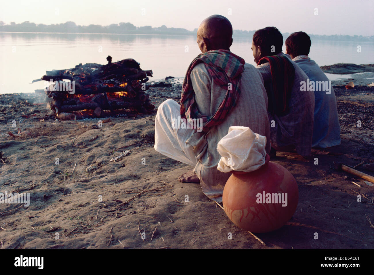 Three figures perform cremation on bank of the River Ganges Varanasi ...