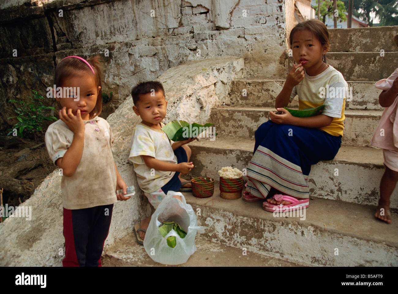 Children sitting on steps and eating from leaf plates in Luang Prabang ...