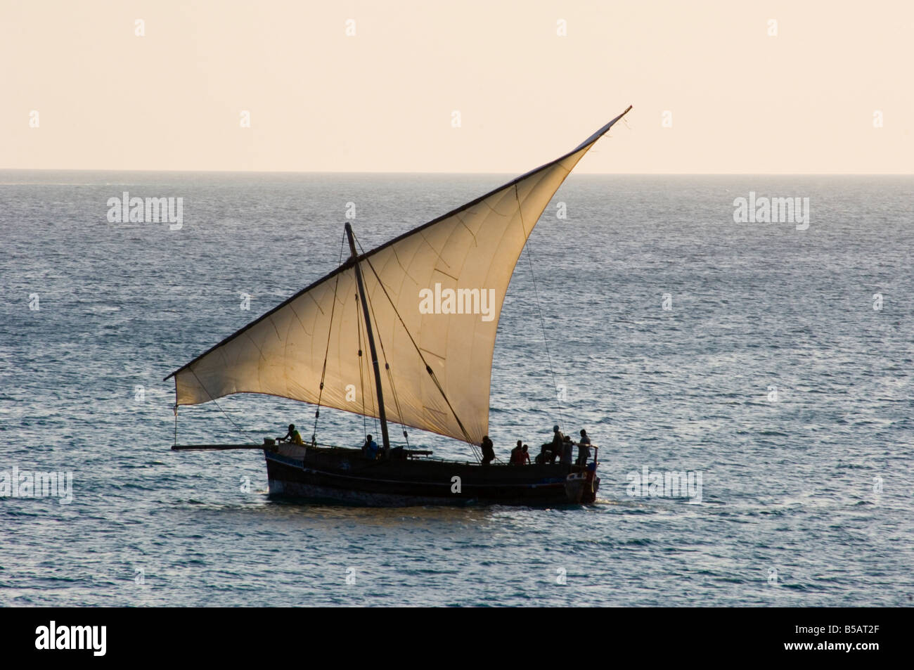 A traditional wooden dhow sailing near Stone Town at sunset Zanzibar ...