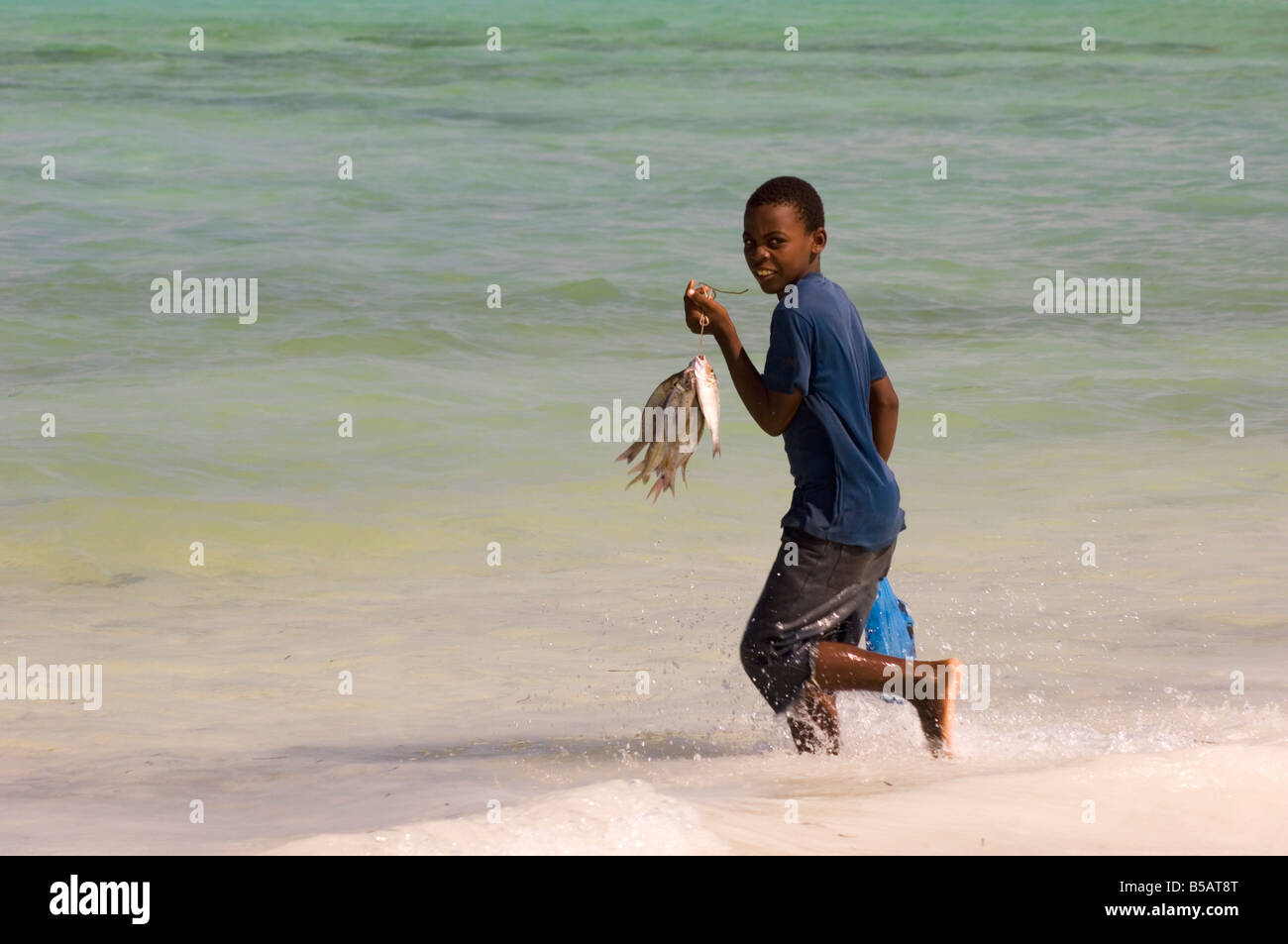 A boy running in the sea with his recently caught fish in hand Jambiani ...