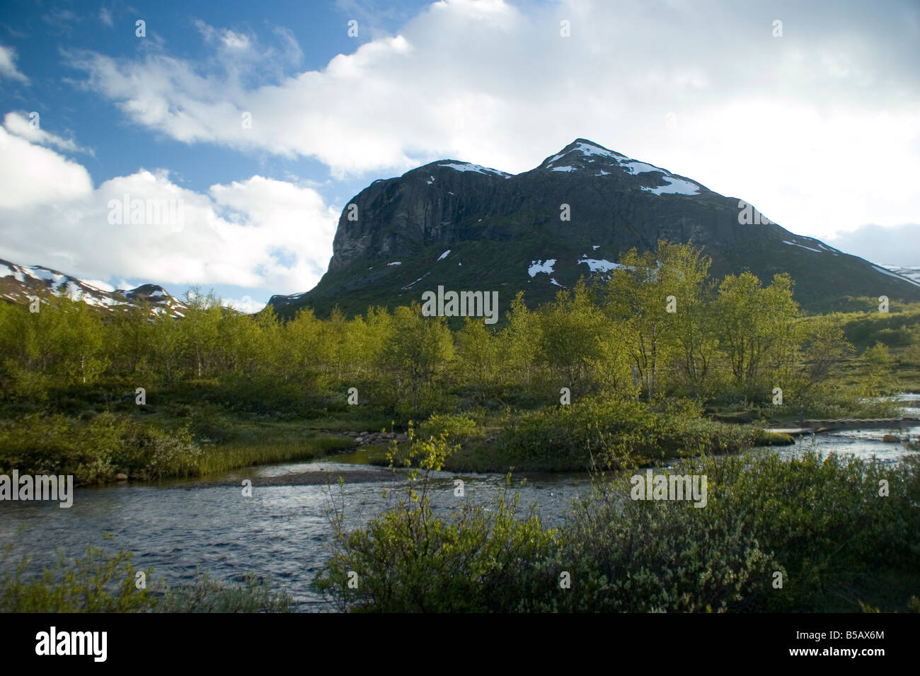 The summer sun casts its light on a mountain and creek at Gjendebu ...