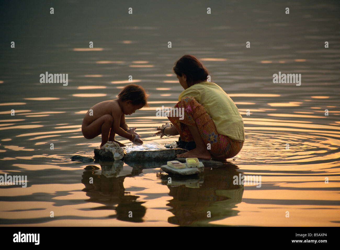 Mother and child silhouetted at dusk washing clothing in Phewa Tal ...