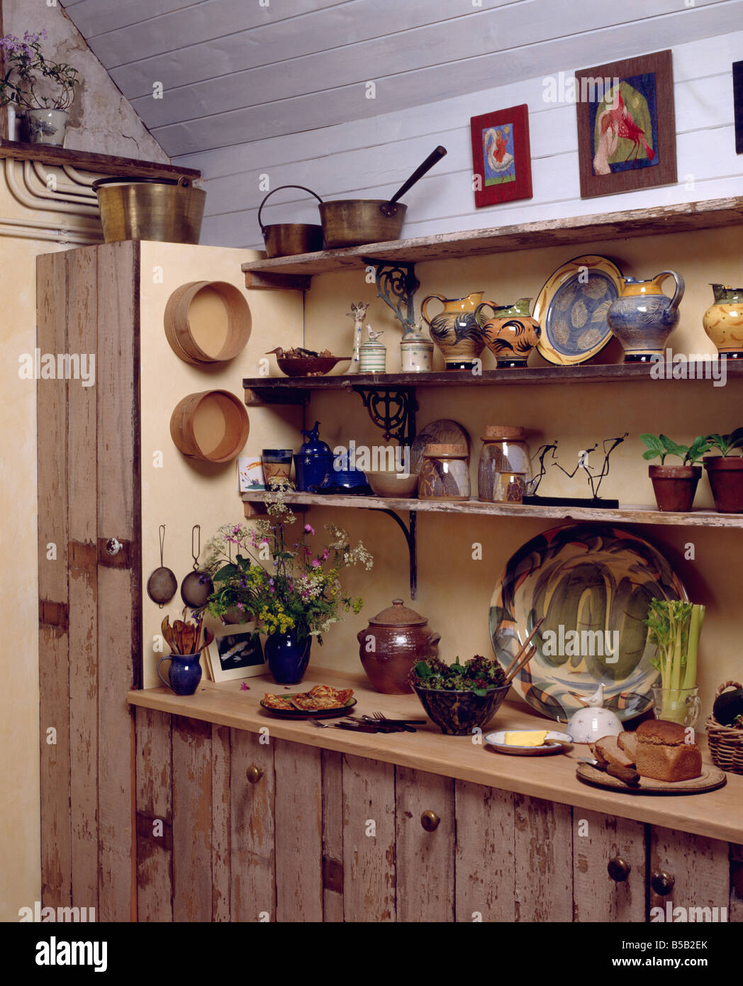 Pottery dishes and jug on shelves in cottage kitchen with rustic wooden ...
