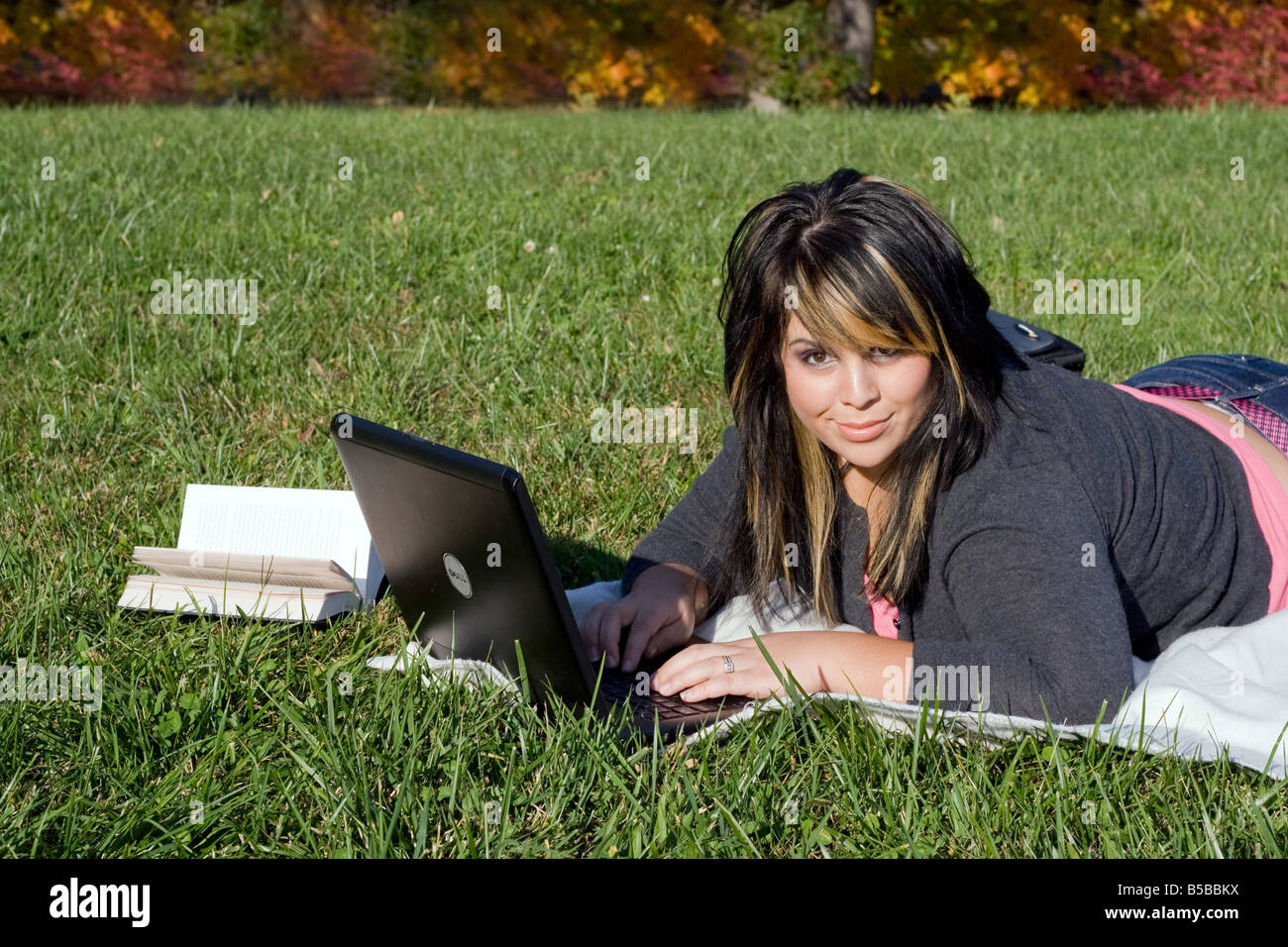 A young student using her laptop computer while laying in the grass on ...