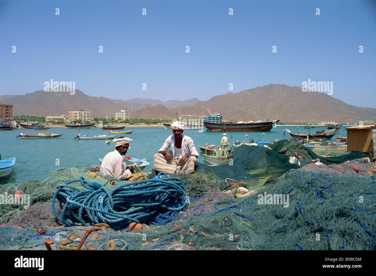 Portrait of men sitting amongst fishing nets at dockside Fujairah ...