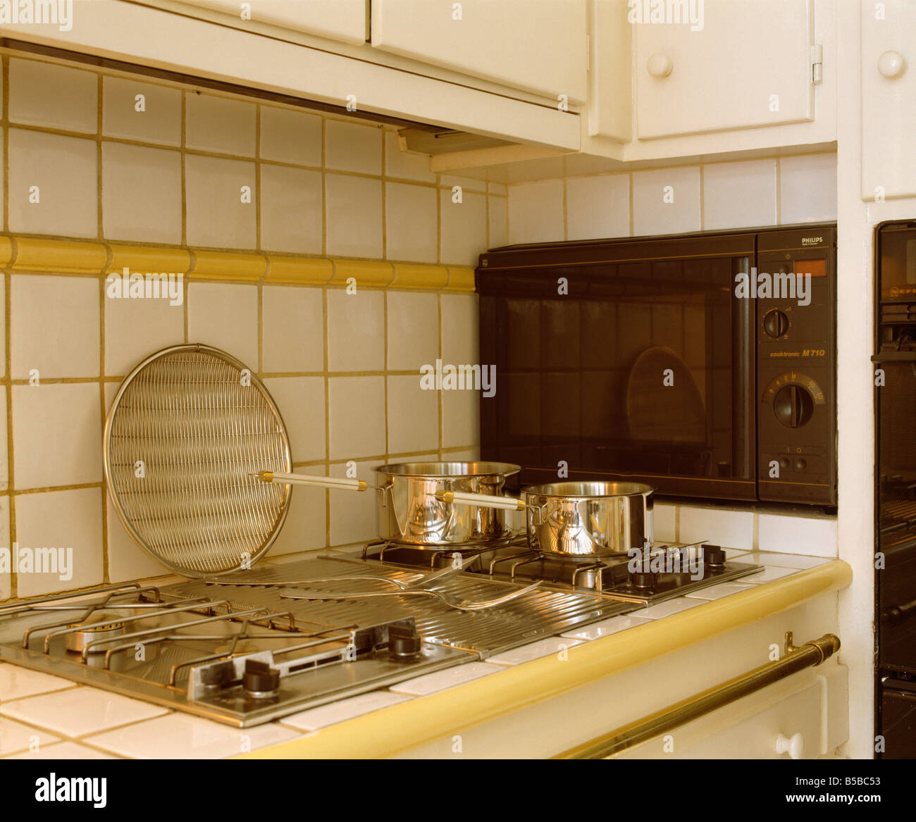 Close-up of white wall tiles above stainless steel pans on steel hob ...