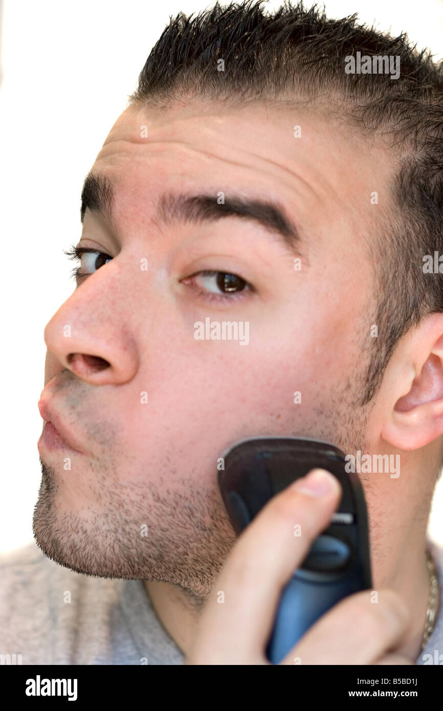 A closeup of a young man shaving his beard off with an electric shaver ...