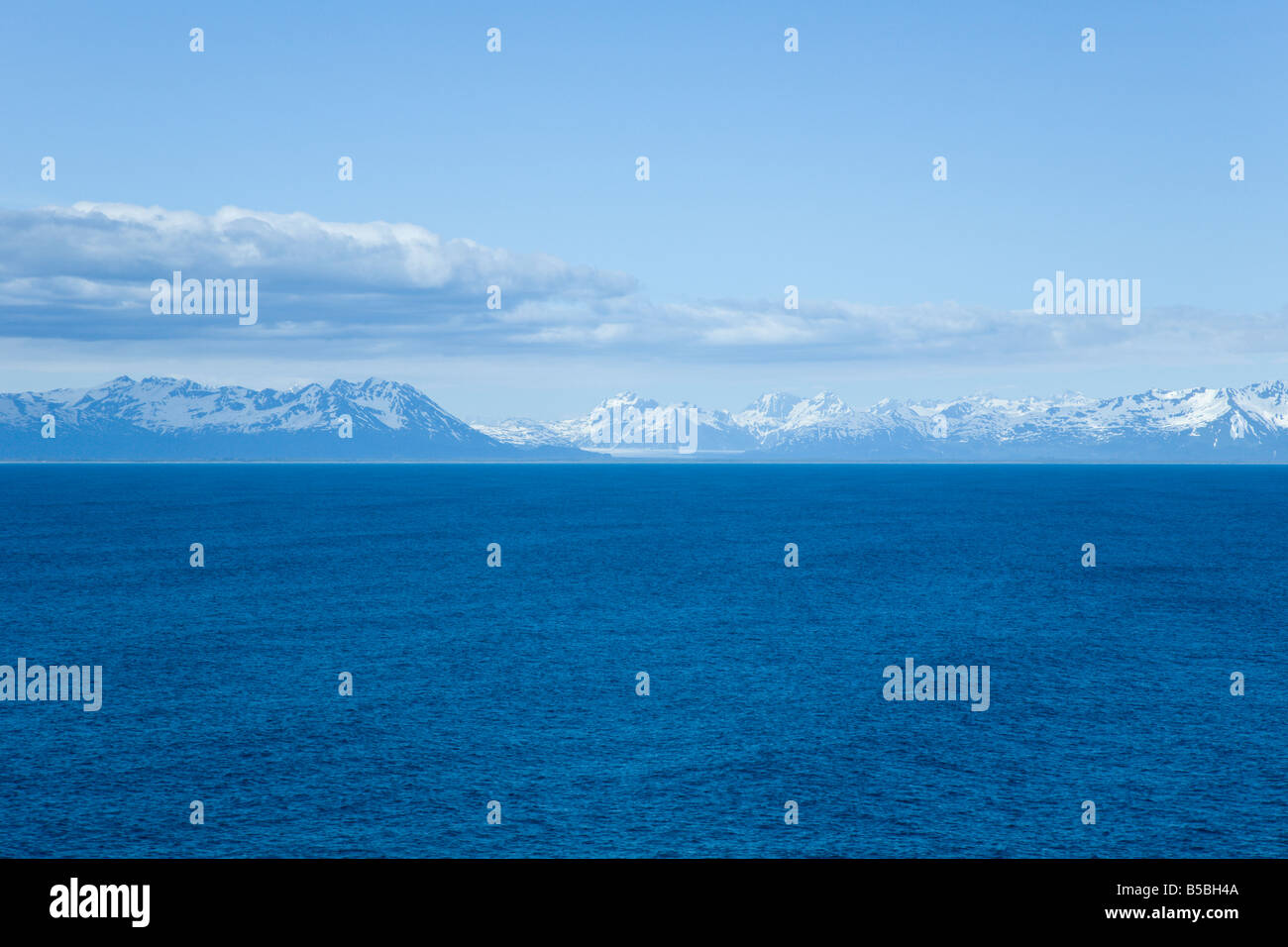 Snow capped mountains and low hanging clouds over deep blue waters of ...