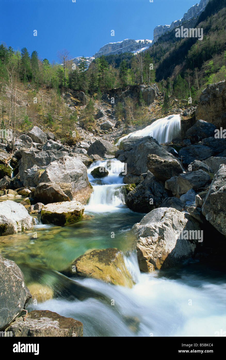 Stream flowing over rocks with trees and mountains in the background in ...