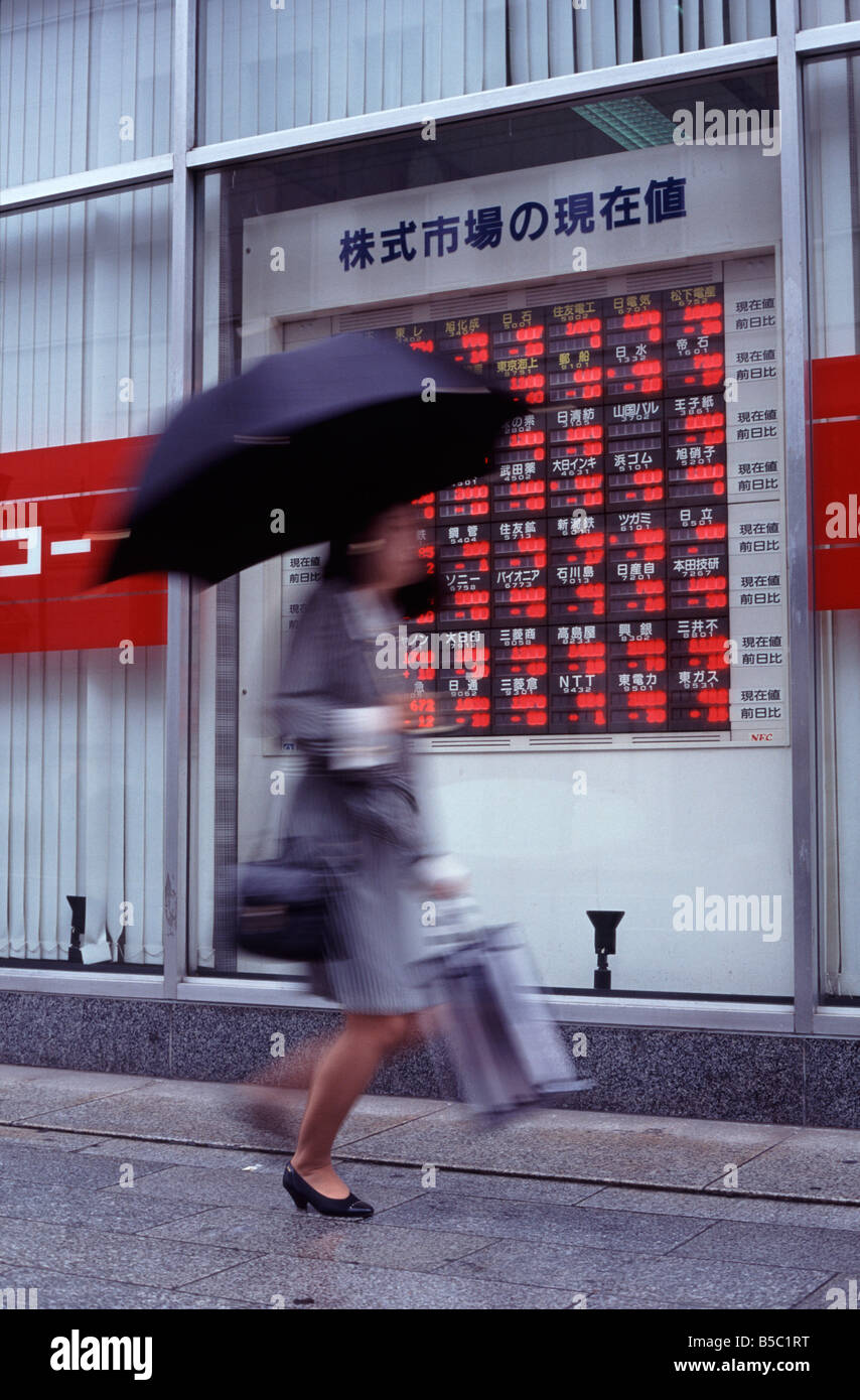 japanese woman walking past japanese stock market trading screen ...