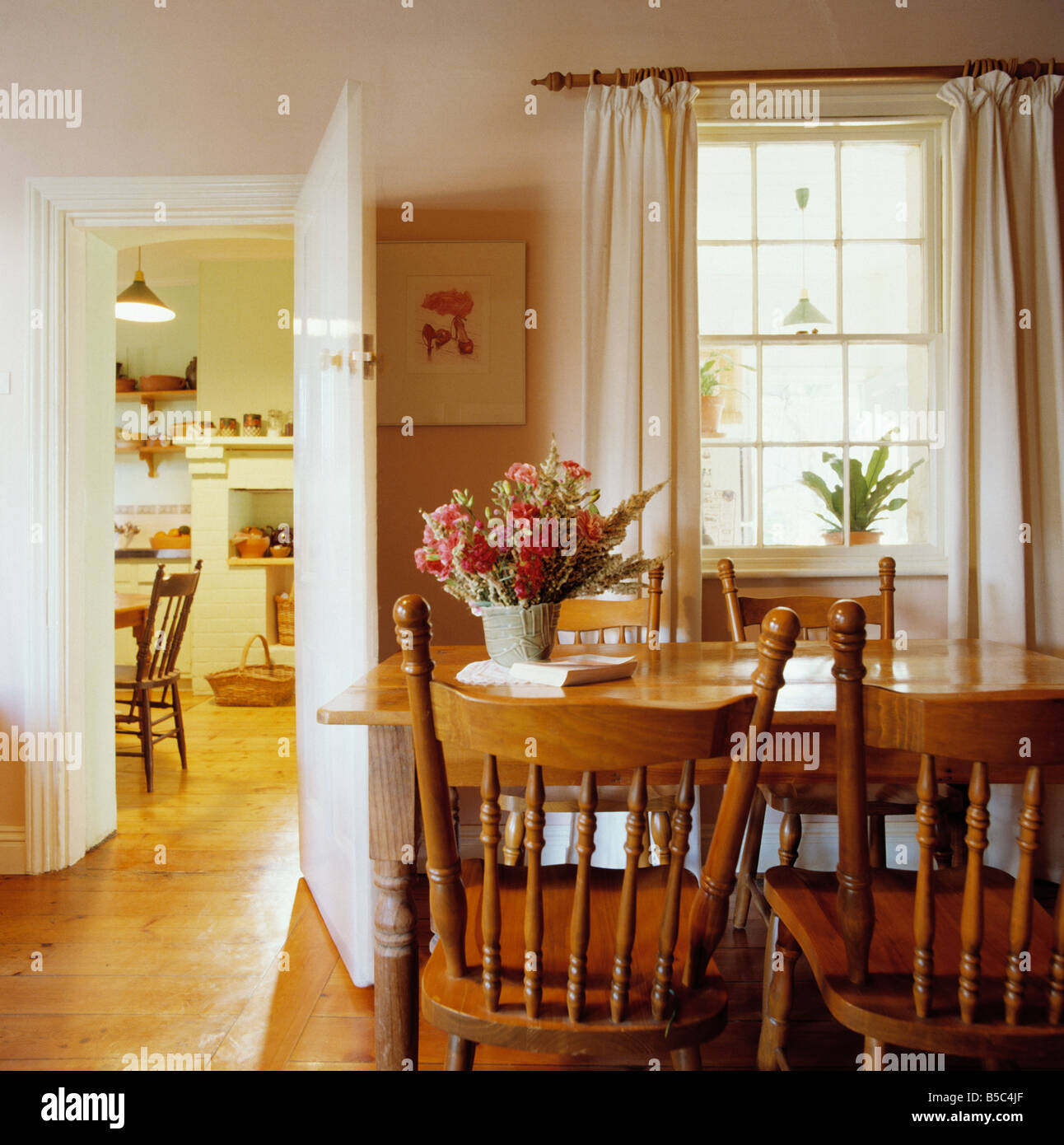 Wooden chairs and polished table in front of window with cream curtains ...