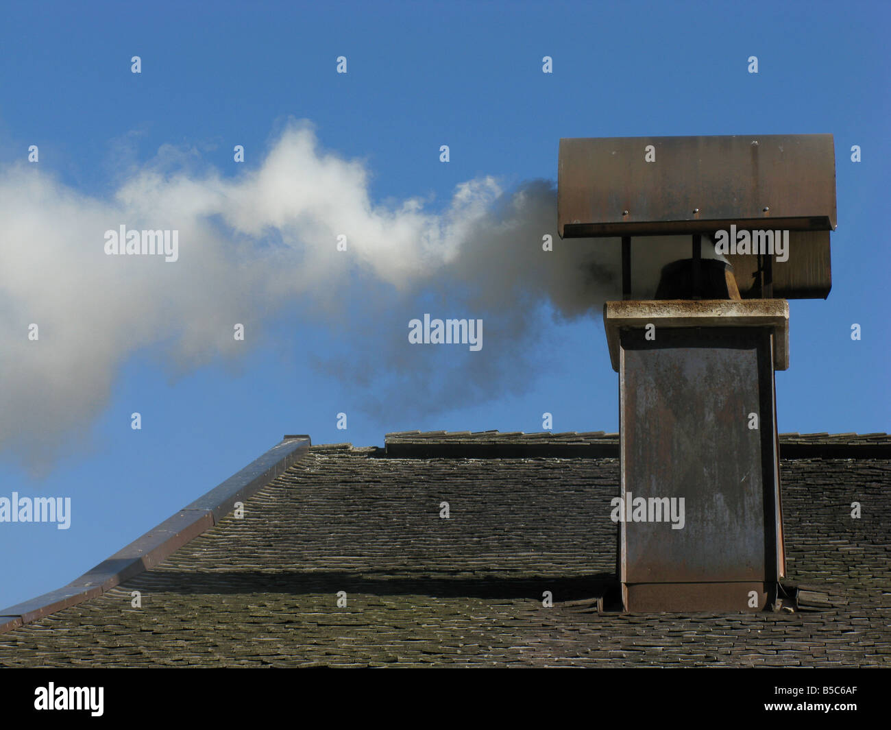 a smoking steel smokestack against blue sky Stock Photo - Alamy