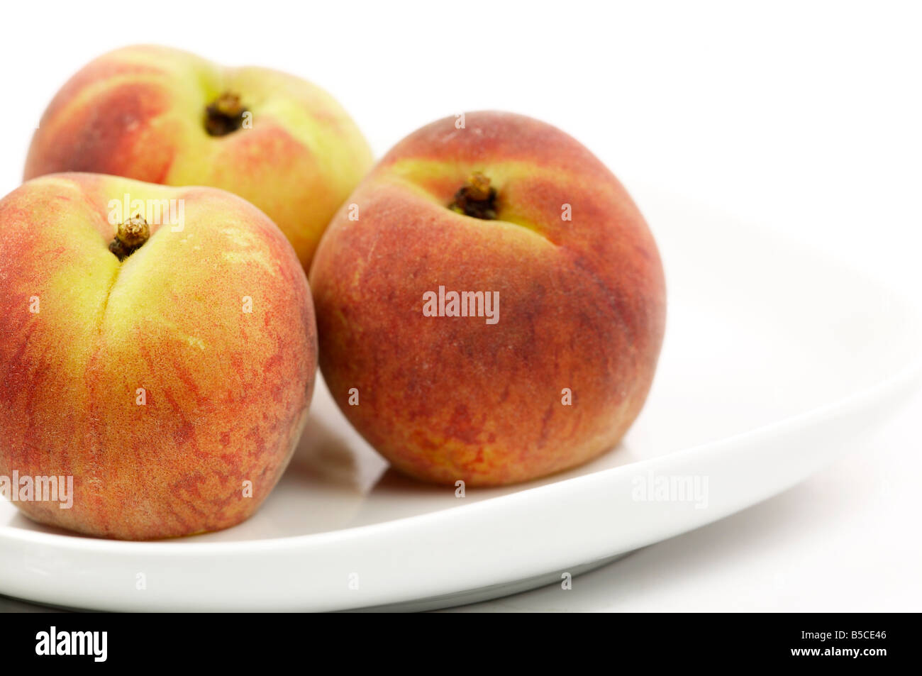 Three Peaches on white plate on white background Stock Photo - Alamy