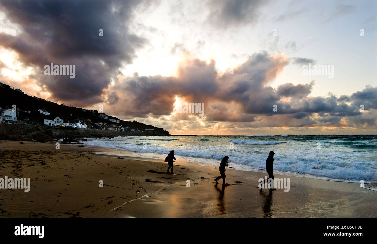Three young people walking across the beach under a dramatic sky at ...