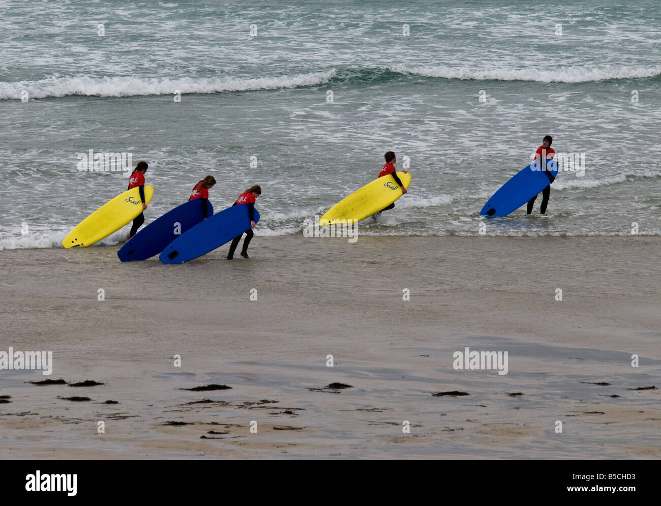 five surfers dragging their surfboards across the beach at Sennen in ...