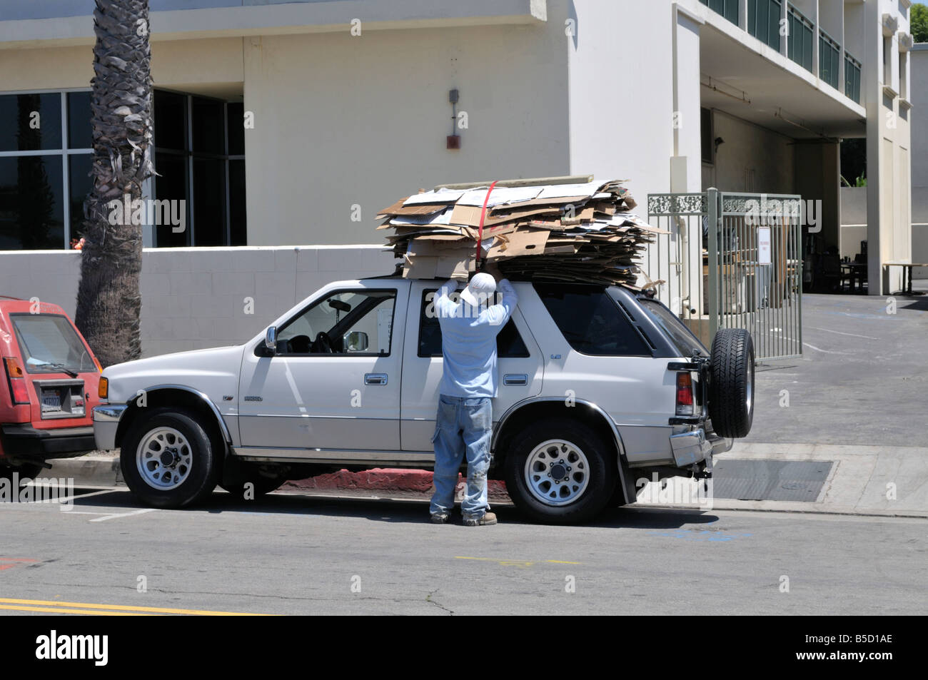 Young man loading a heap of packaging material on top of his vehicle ...