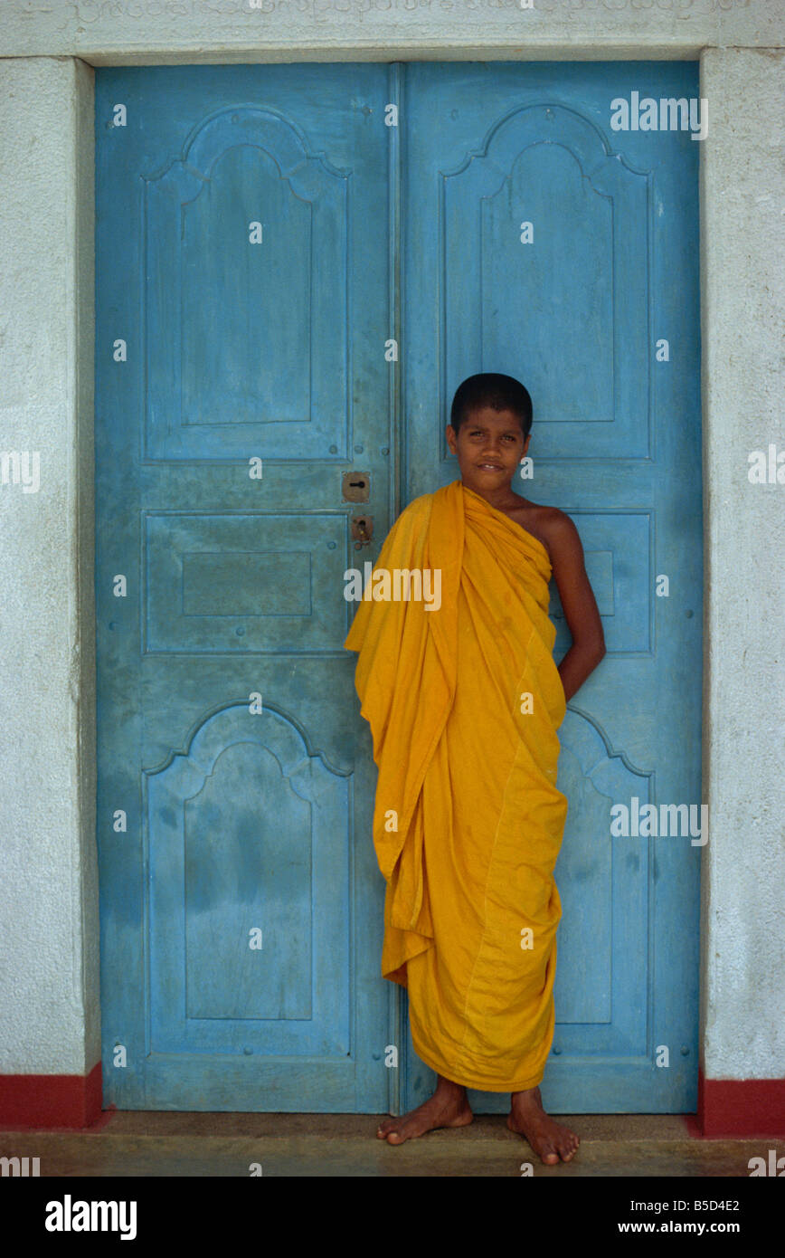 Young Buddhist monk in saffron robe in front of a blue door near Kandy ...