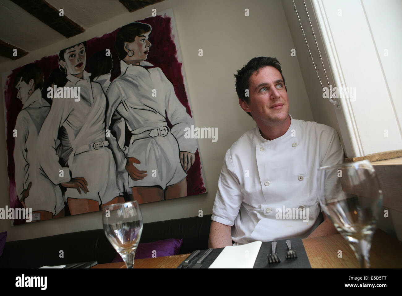 a portrait of a handsome chef in his chef whites sitting on a table in ...