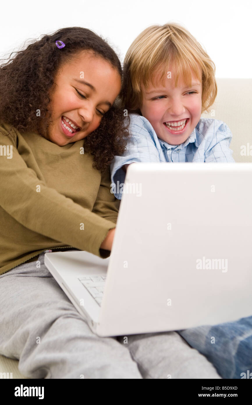 Two young children having fun on a laptop while sitting on a settee ...