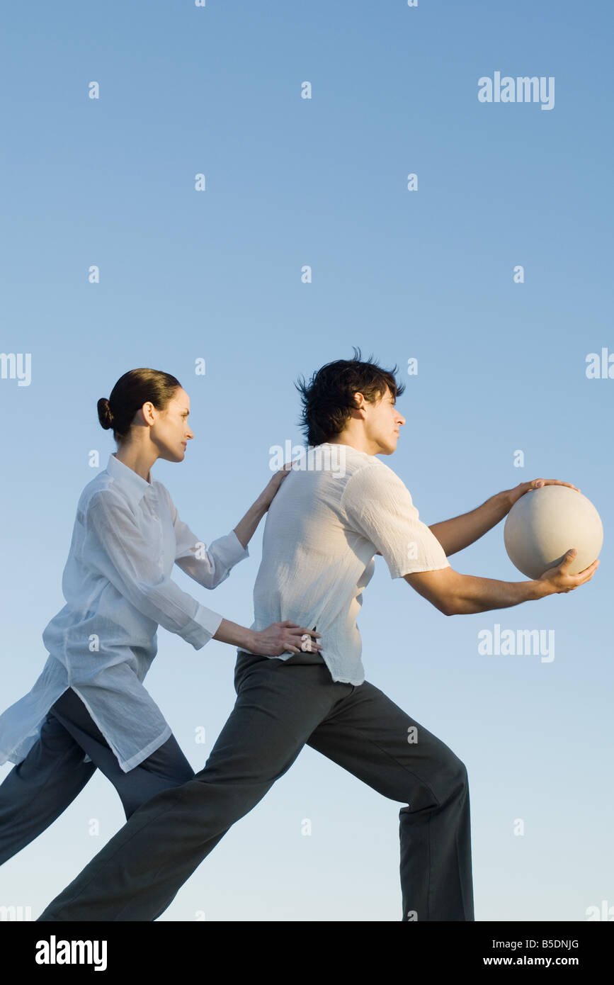 Man holding out ball, woman standing behind, hands on hip and shoulder ...