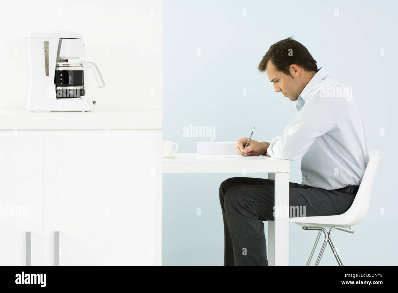 Man sitting at desk writing, side view Stock Photo - Alamy