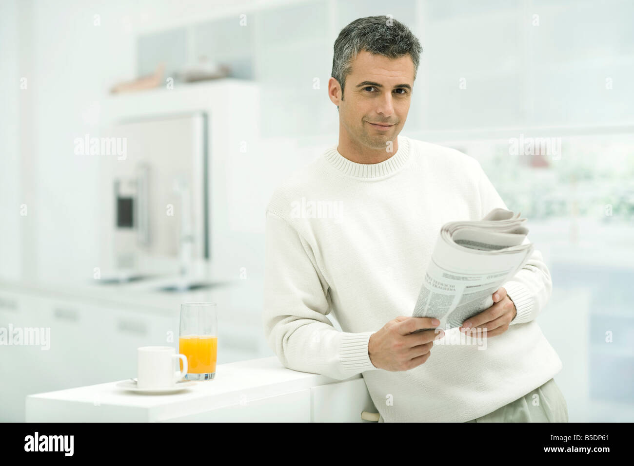 Man leaning against kitchen counter, holding newspaper, smiling at ...