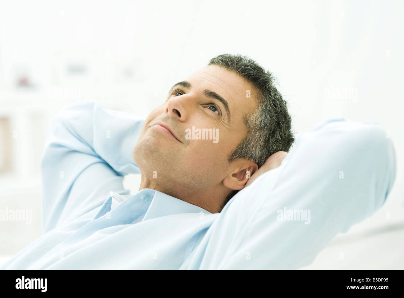 Man leaning back with hands behind head, looking up and smiling Stock ...