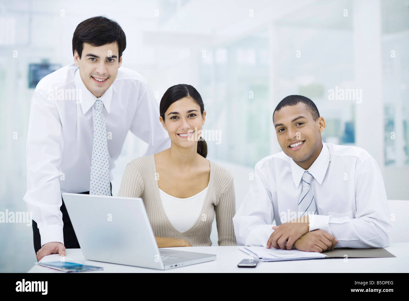 Professionals gathered around laptop computer, smiling at camera Stock ...