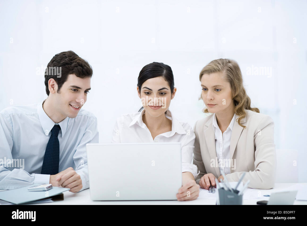 Three professionals looking at laptop computer together, smiling Stock ...