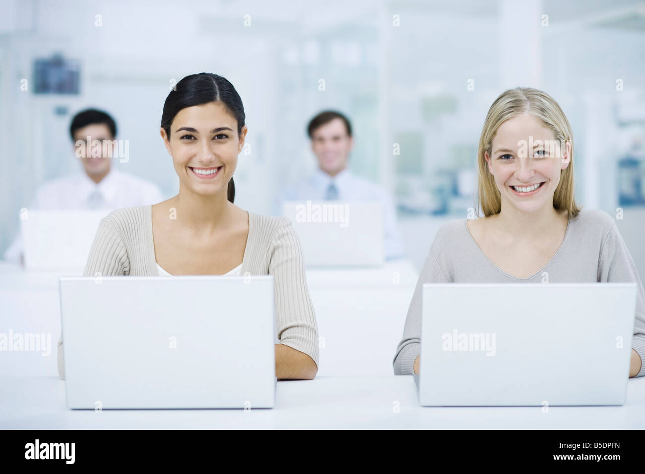 Professional women using laptop computers, smiling at camera ...