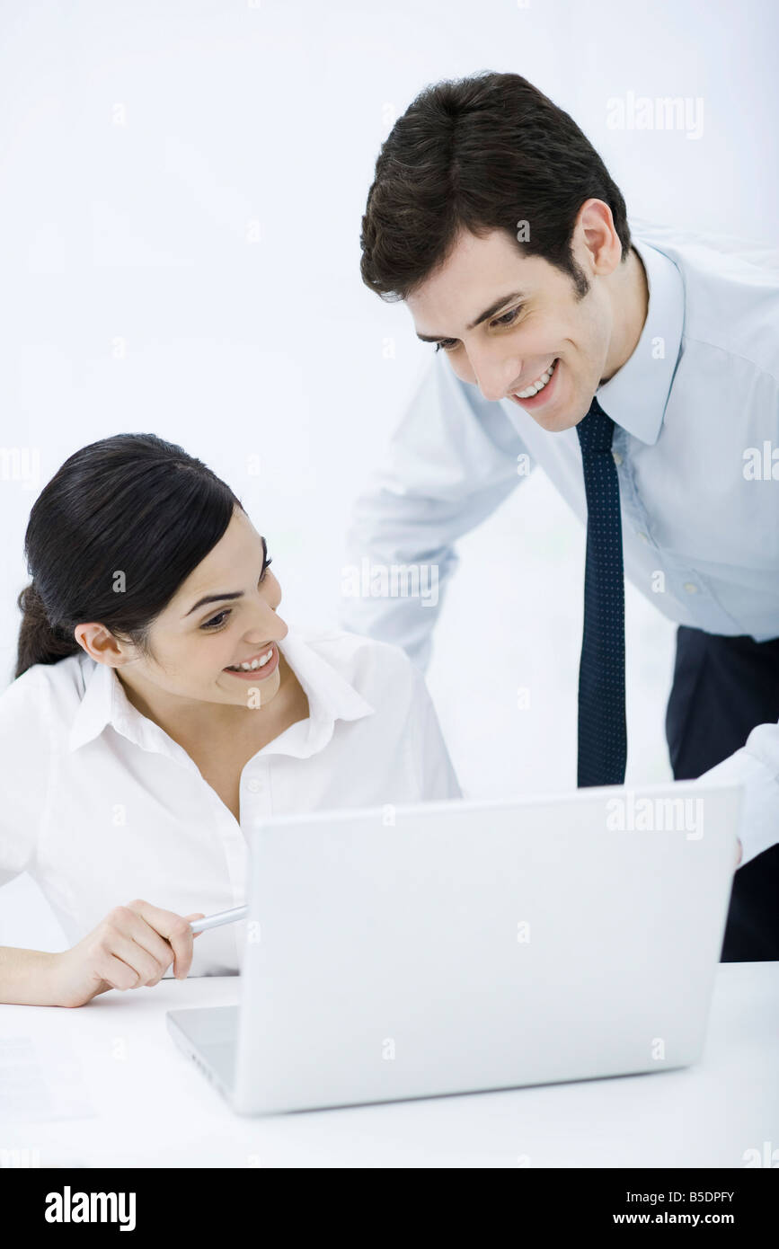 Professional man looking over female colleague's shoulder at laptop ...