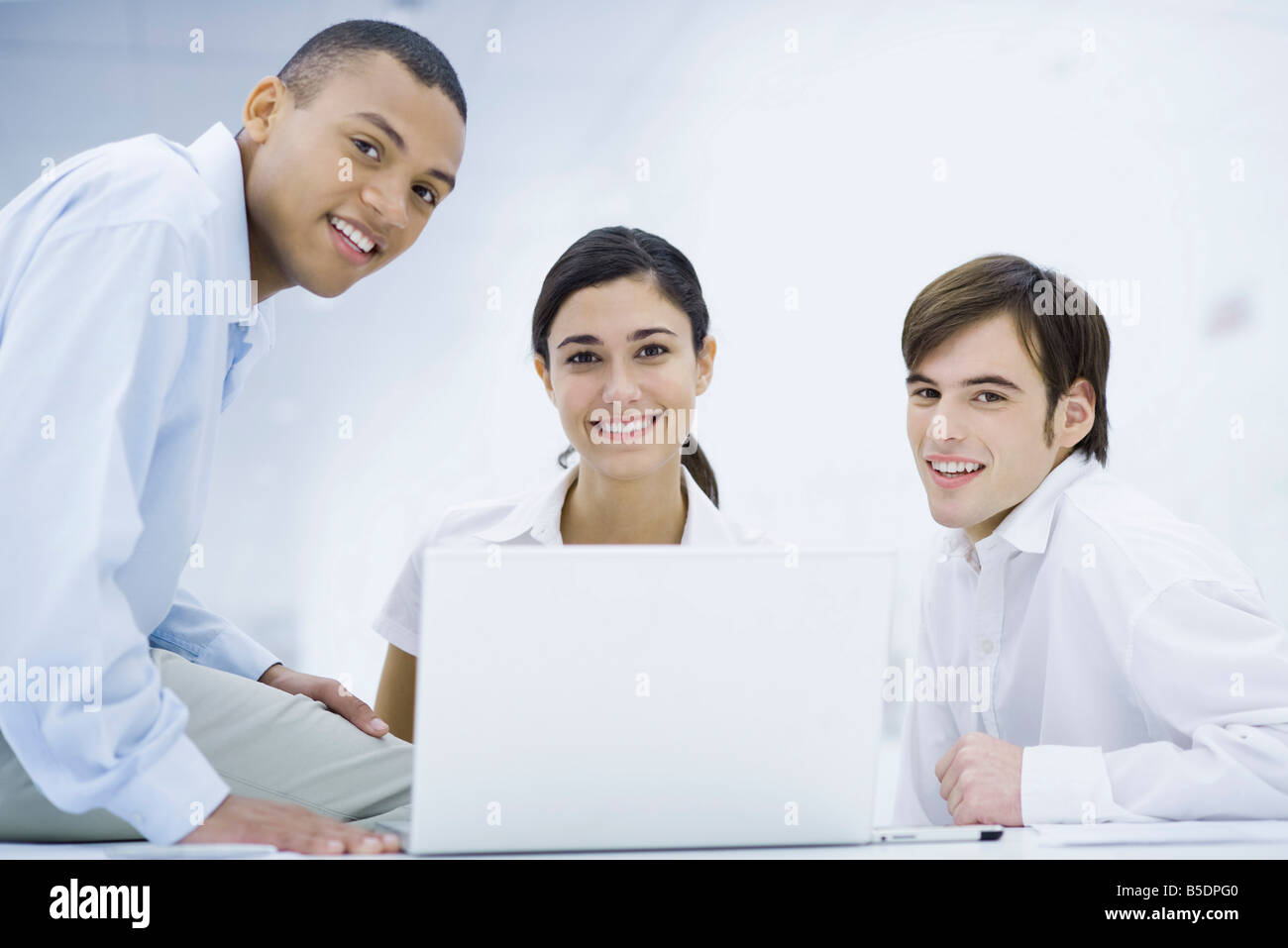 Young professionals gathered around laptop computer, smiling at camera ...