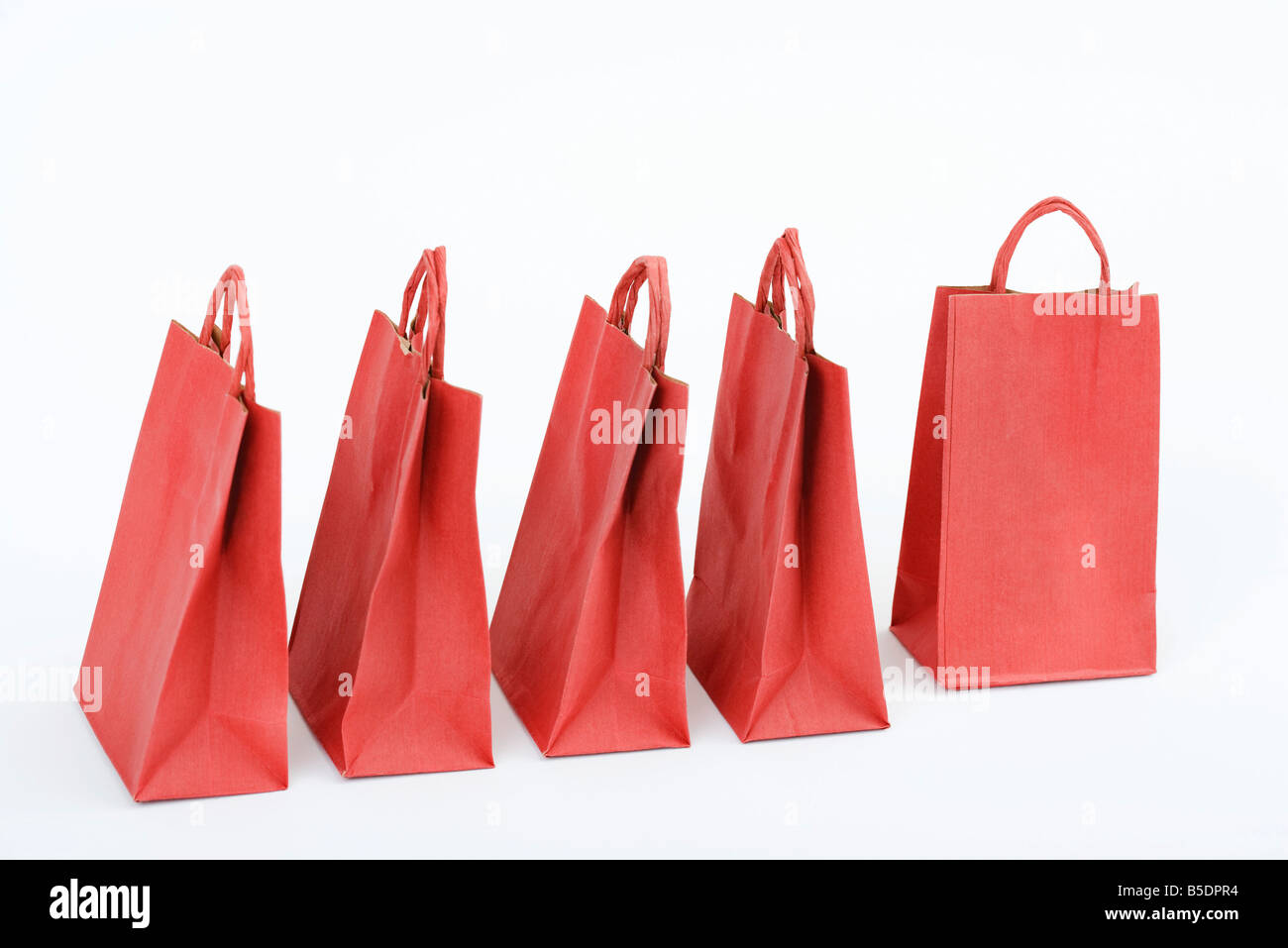 Five red shopping bags arranged side by side, one turned at right angle ...