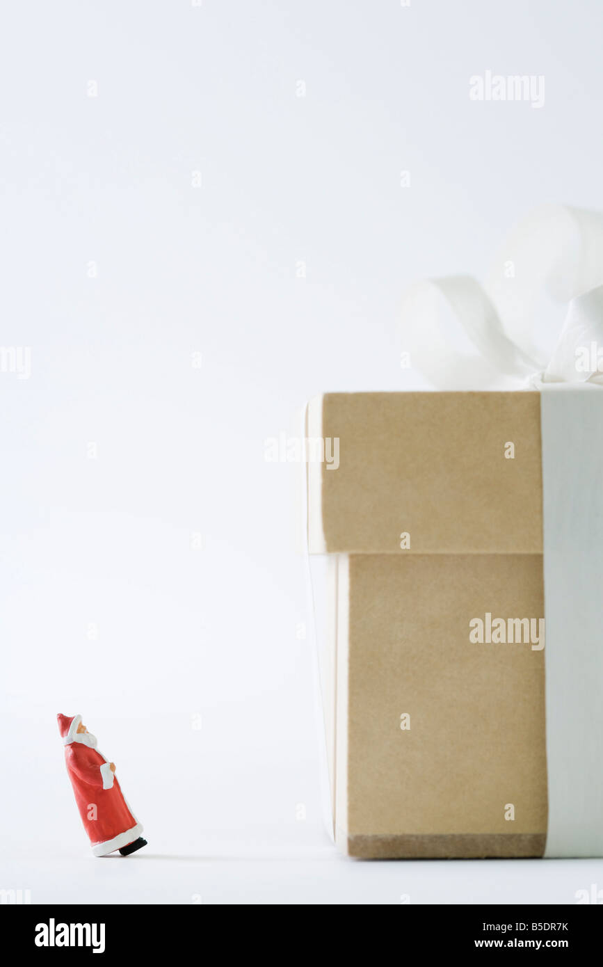 Miniature Santa Claus looking at large gift, side view Stock Photo - Alamy