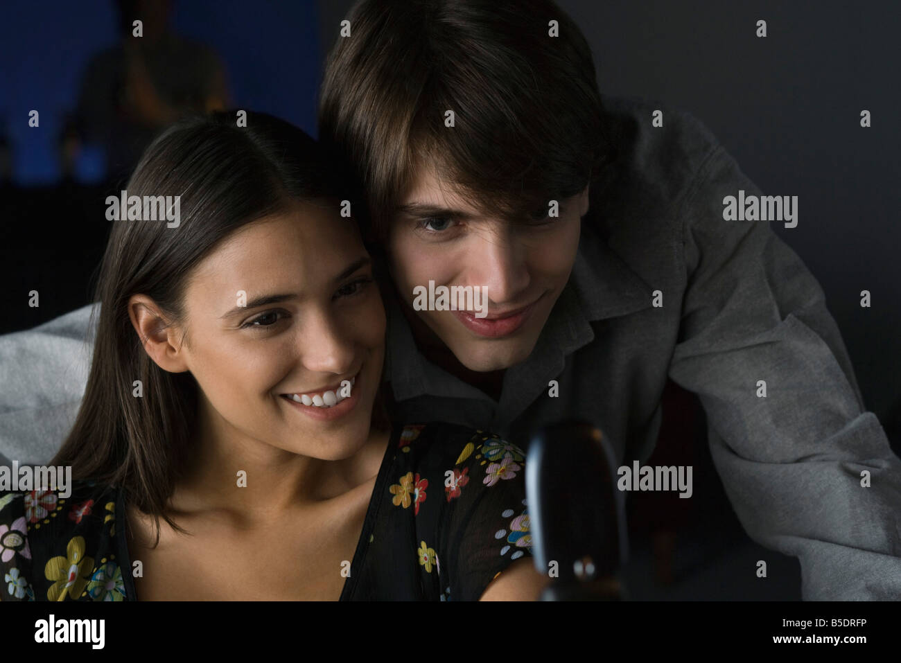 Couple together looking at cell phone, man leaning over woman's ...