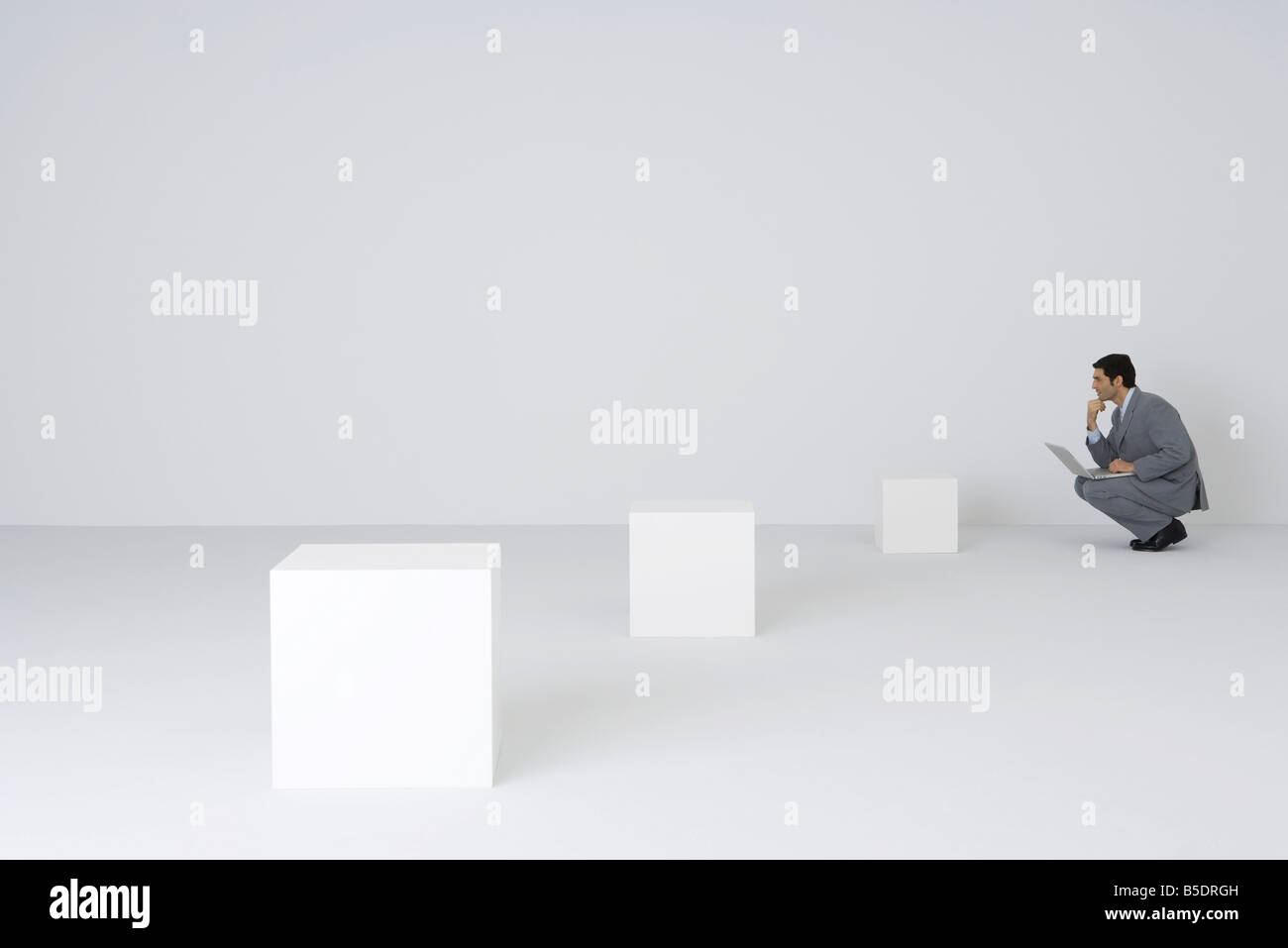 Businessman squatting using laptop, looking at empty pedestals Stock ...