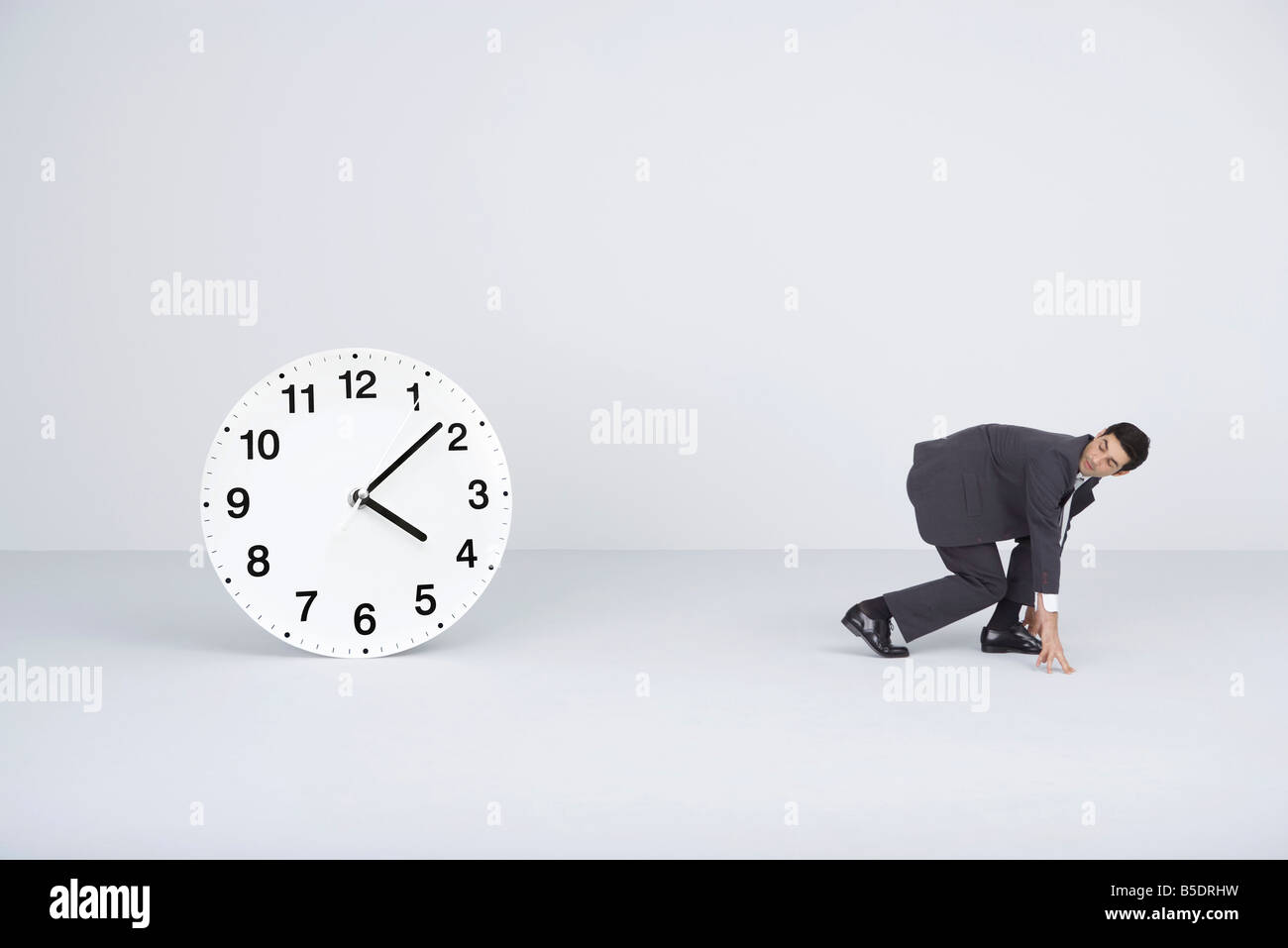 Businessman racing against time, looking over shoulder at large clock ...