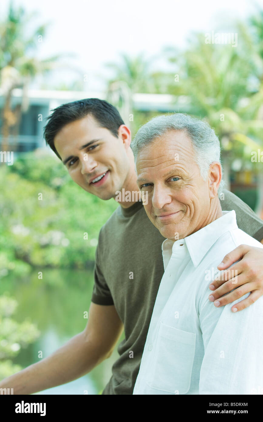 Young man with arm around father's shoulder, both smiling, portrait ...