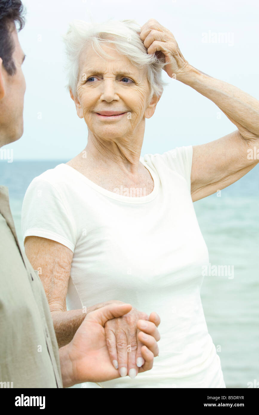 Senior woman scratching head and holding adult son's hand, sea in ...