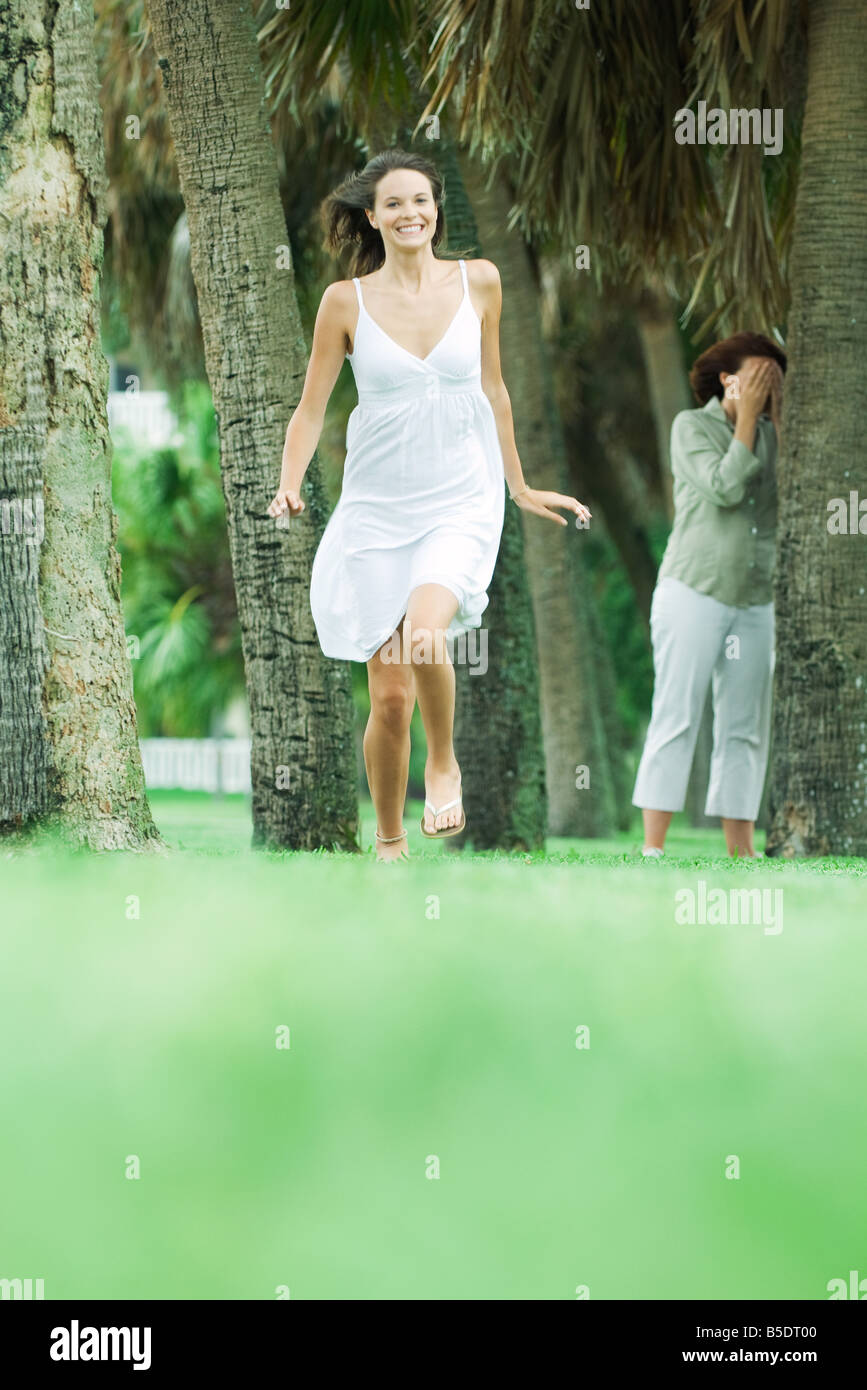Mother and teen daughter playing hide-and-seek in park, girl running ...