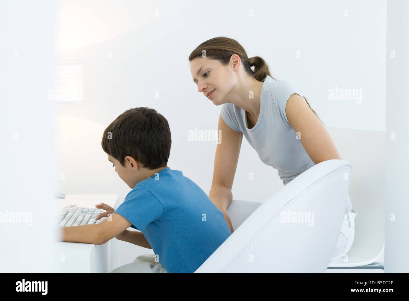 Boy typing on keyboard, mother looking over shoulder Stock Photo - Alamy