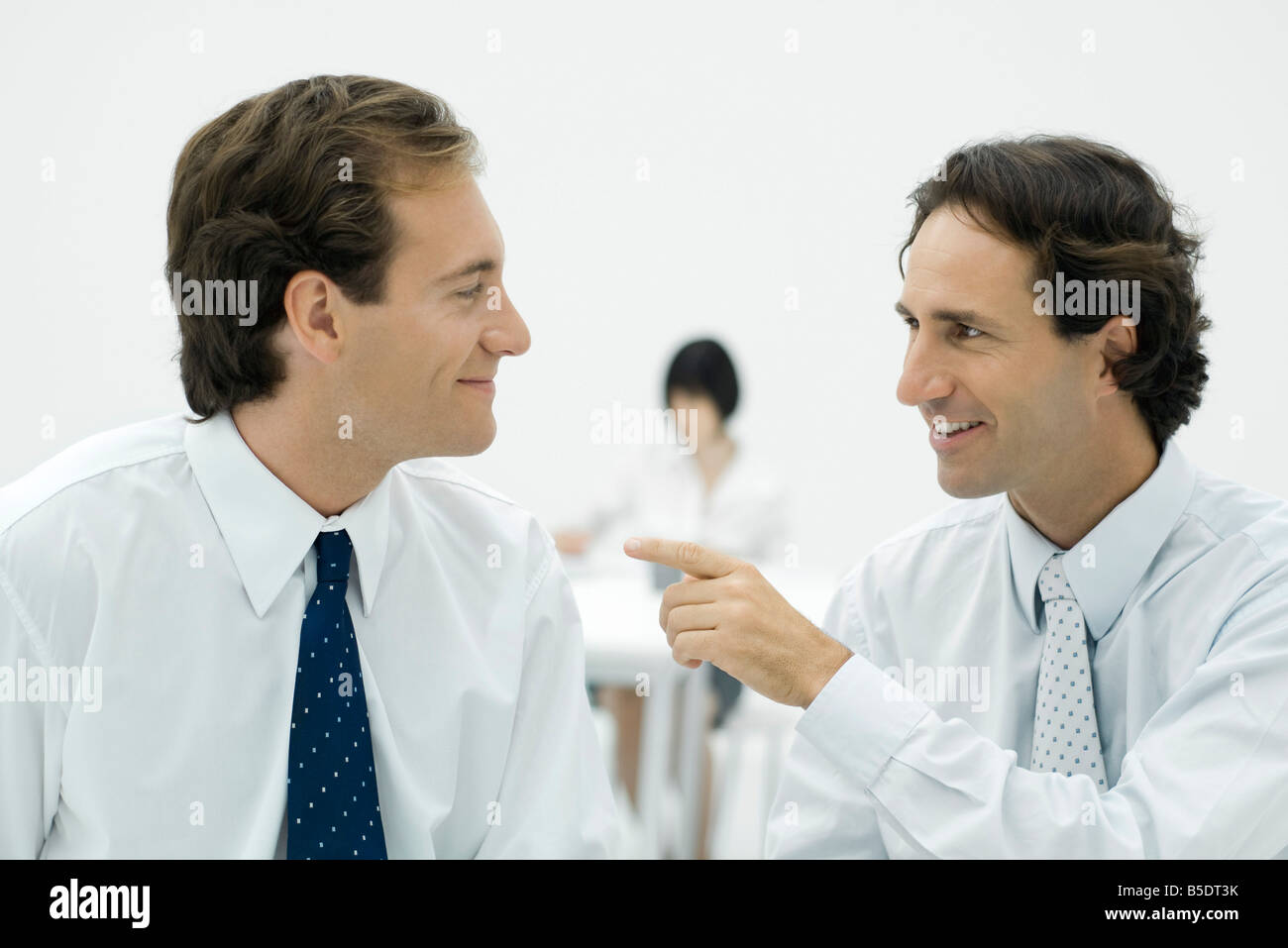 Professional men smiling at each other, one man pointing Stock Photo ...