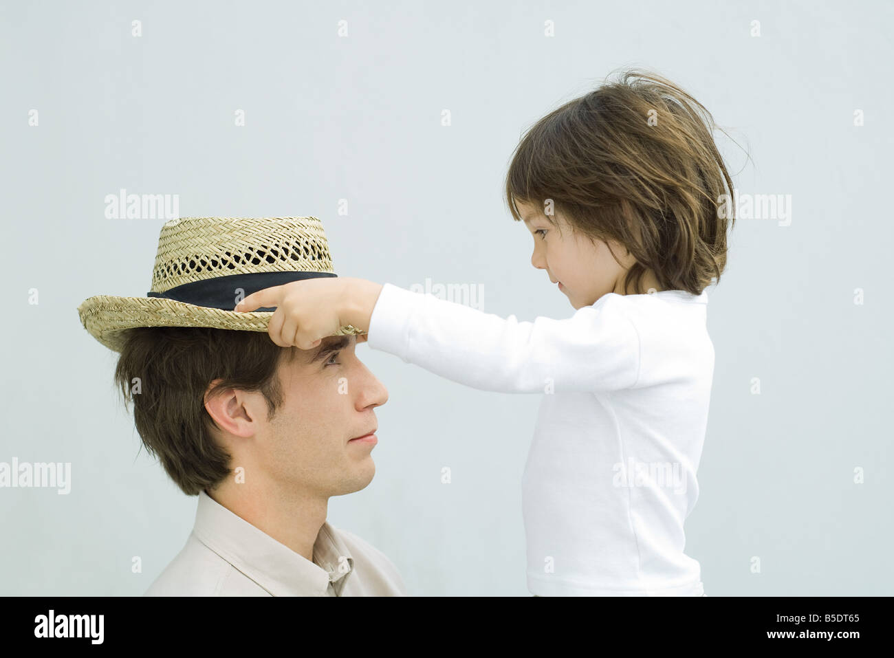 Little boy putting straw hat on his father's head, side view Stock Photo - Alamy