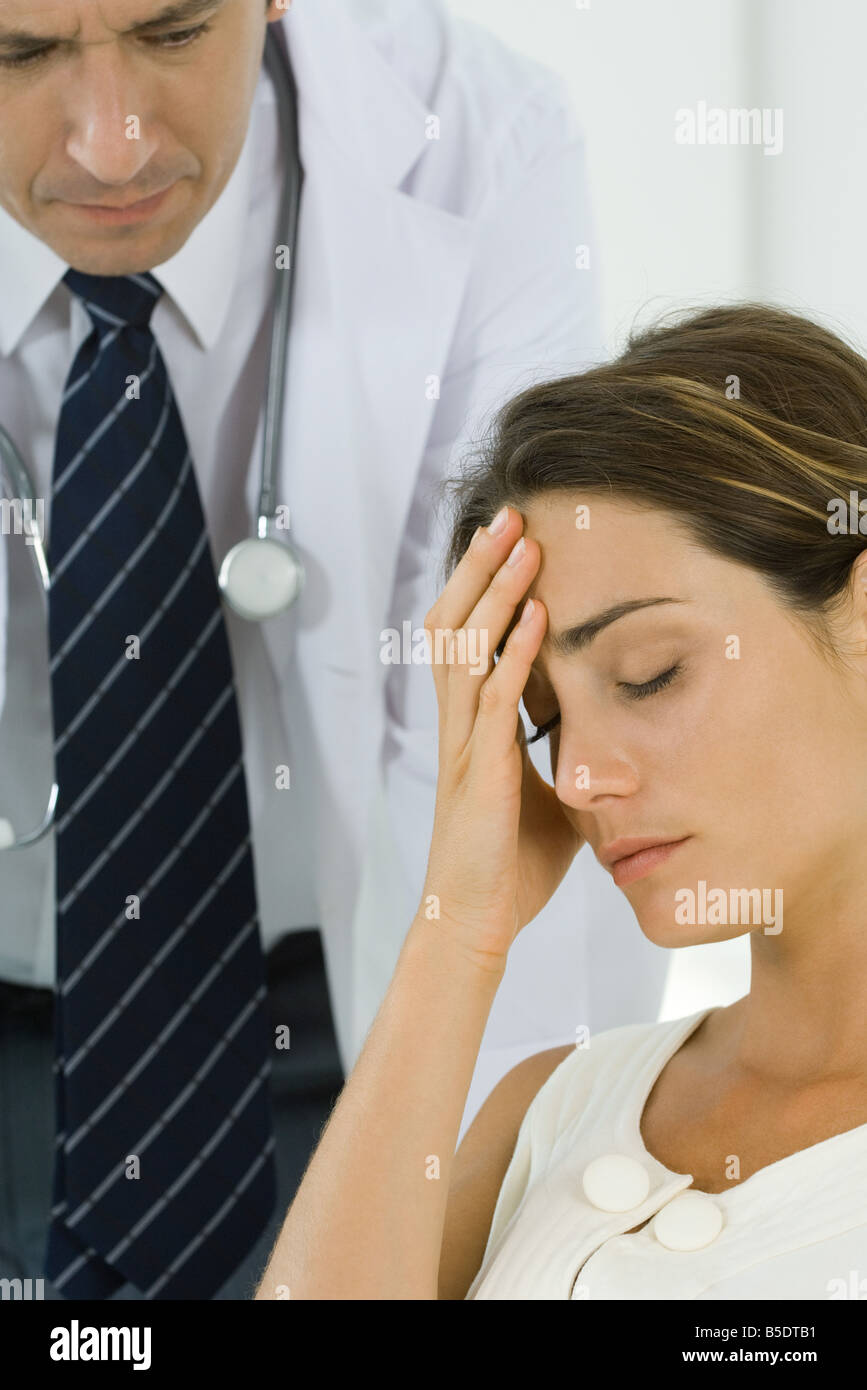 Woman holding head, doctor leaning behind her Stock Photo - Alamy