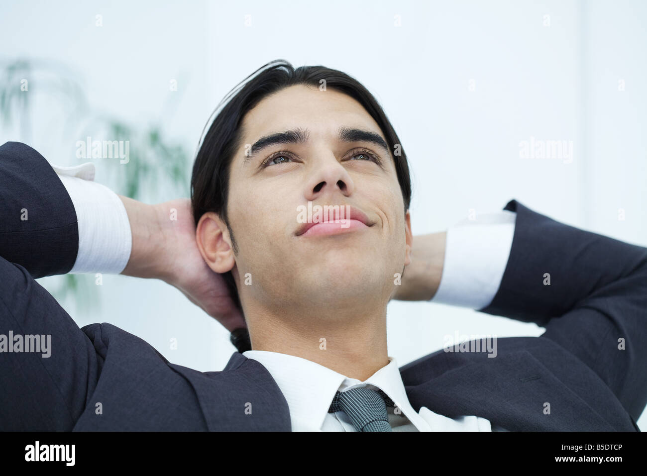 Young businessman leaning back with hands behind head, looking up ...