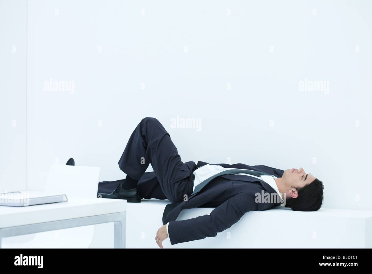 Businessman lying down on ledge in office Stock Photo - Alamy