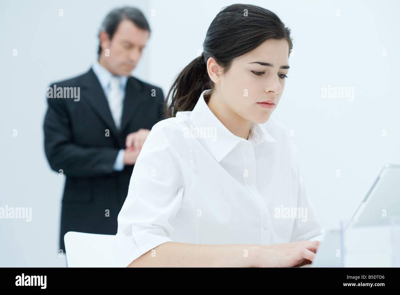Young woman typing on laptop, boss checking time in background Stock ...