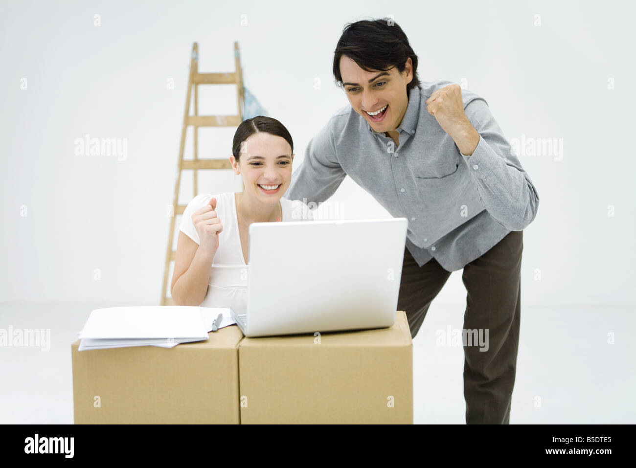 Young couple looking at laptop computer on top of cardboard box ...