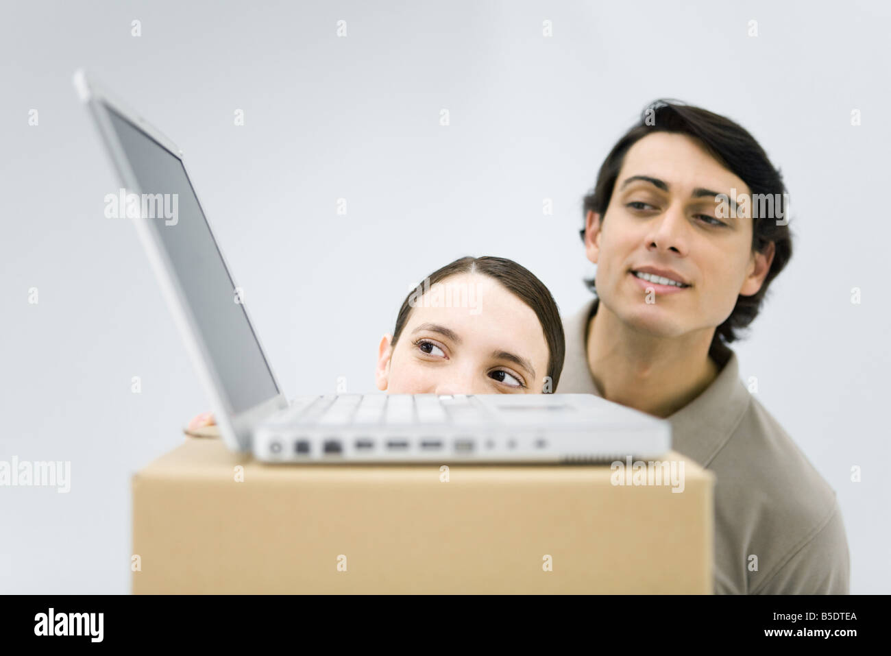 Man and woman peeking at laptop computer sitting on top of cardboard ...