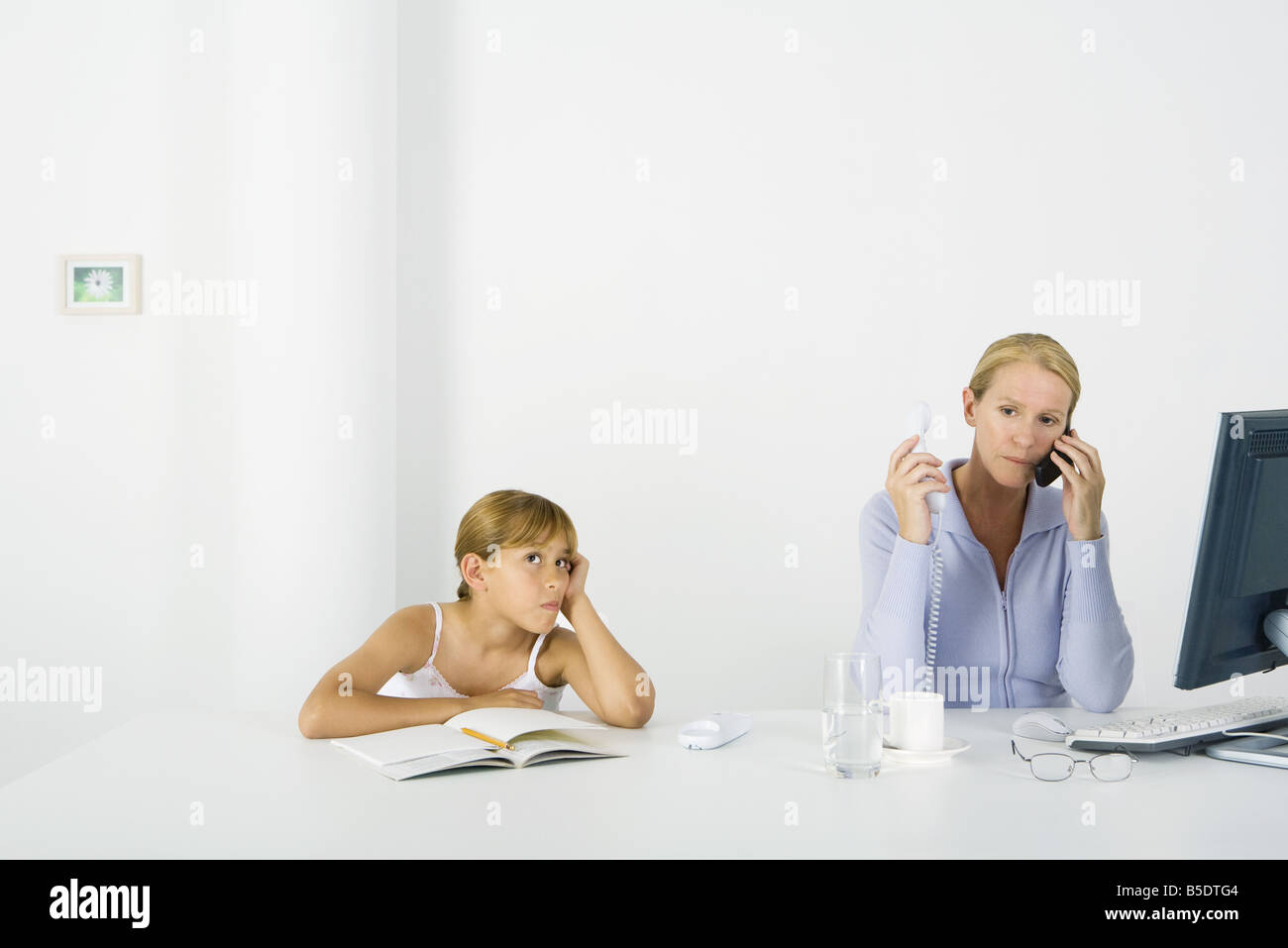 Woman sitting in front of computer, using cell phone and landline phone ...